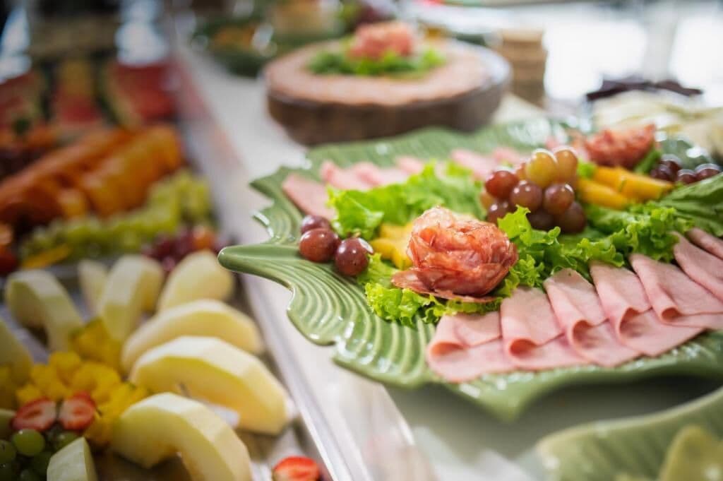 Buffet com diversas opções de comida, incluindo frutas fatiadas, legumes e carnes.