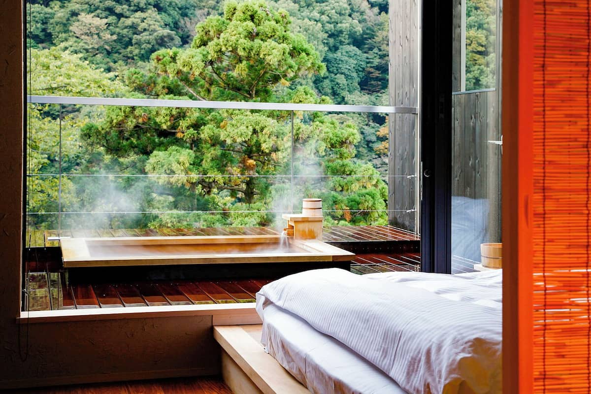 Quarto com uma janela grande, um banco de madeira e uma banheira de hidromassagem lá fora.