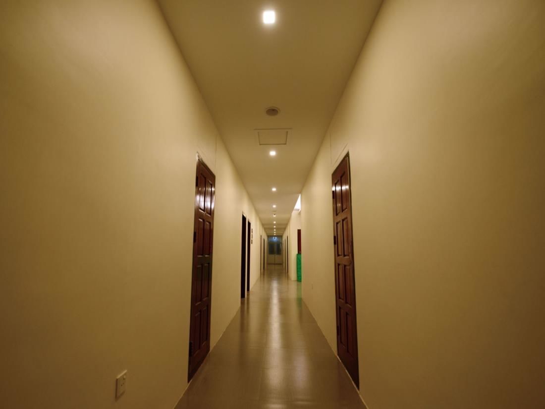 Um corredor comprido e estreito, com portas de madeira em ambos os lados e chão de cor clara.