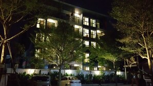 Um edifício moderno com vários andares, janelas iluminadas e cercado por árvores.