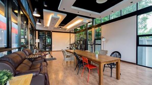 Uma sala de conferências moderna com sofás de couro, uma mesa de madeira e cadeiras. Grandes janelas oferecem luz natural e vista para o verde lá fora.