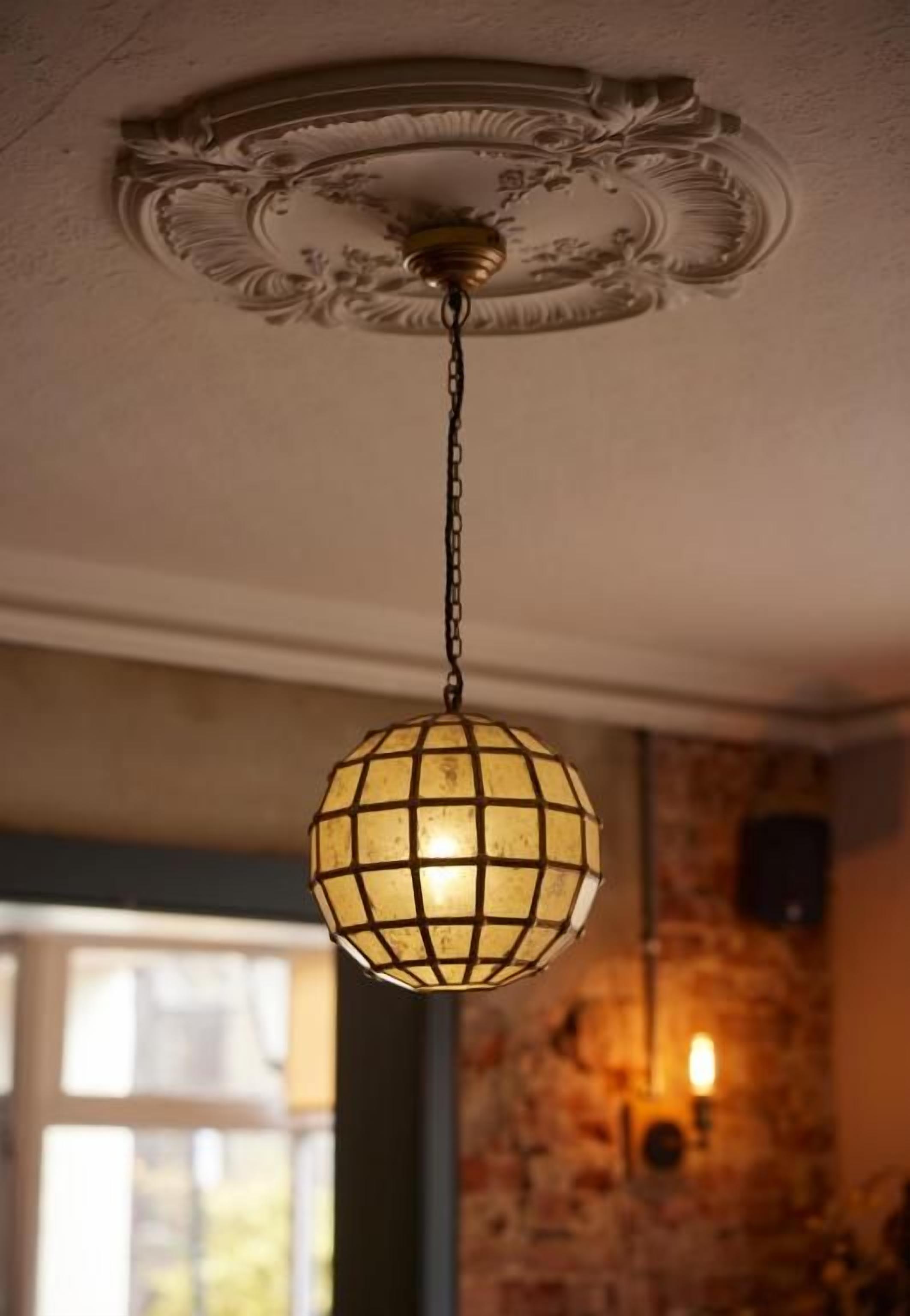 Luminária pendente com padrão quadriculado, uma moldura decorativa no teto e uma parede de tijolos.