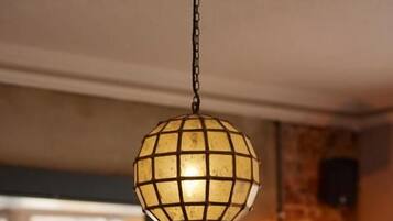 Luminária pendente com padrão quadriculado, uma moldura decorativa no teto e uma parede de tijolos.