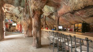 Interior com área de bar, assentos e uma grande formação rochosa.