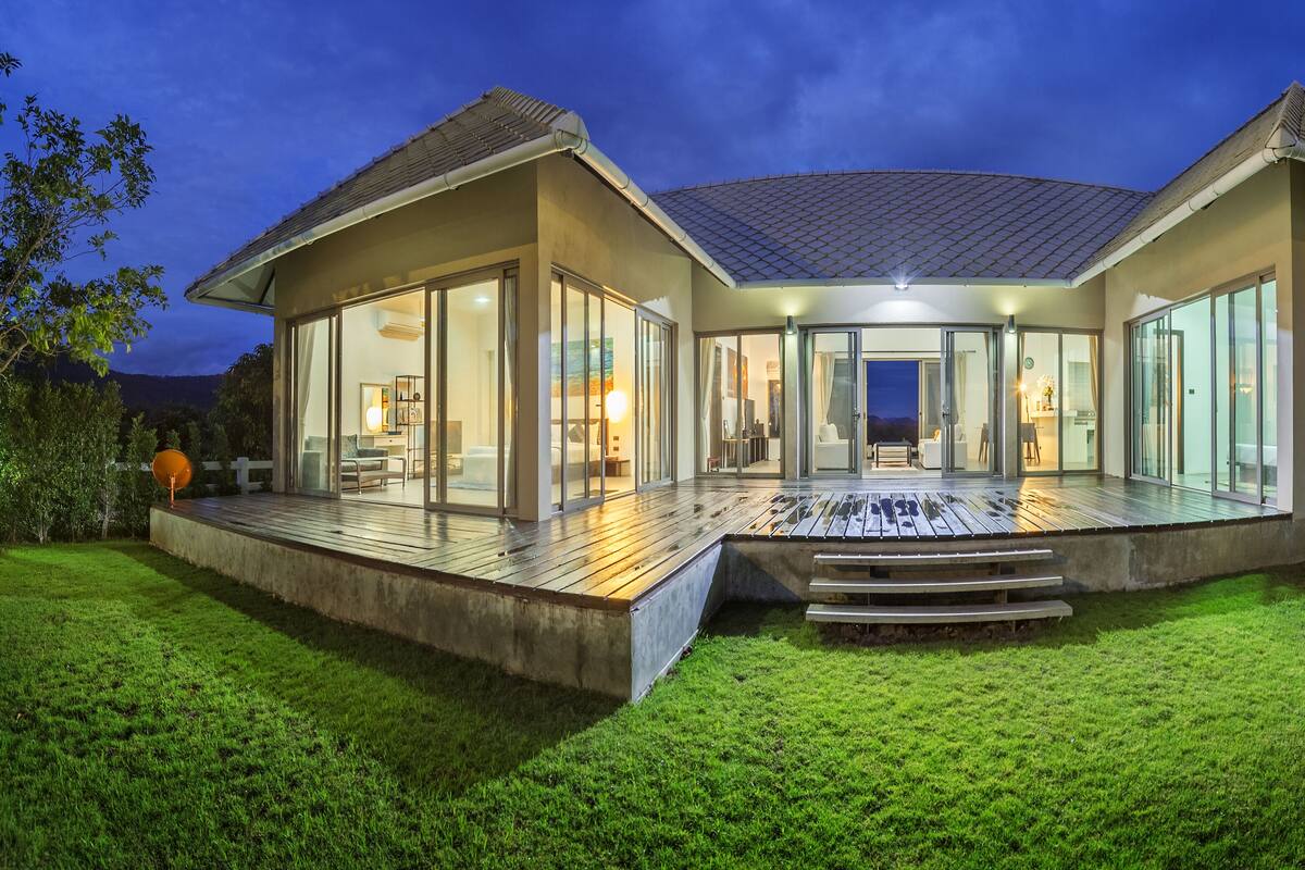 Uma casa moderna com um deck amplo, portas de vidro e um gramado bem cuidado.