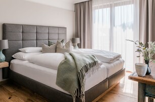 Quarto moderno com uma cama grande, mesa de cabeceira com abajur e janela com cortinas.