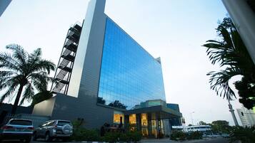 Um hotel moderno com fachada de vidro, entrada imponente e área de estacionamento com carros.