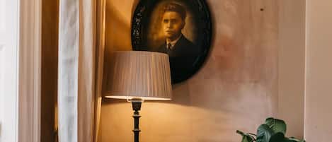 Um quarto acolhedor com poltrona branca, mesa de vidro, abajur, retrato emoldurado e planta em vaso.