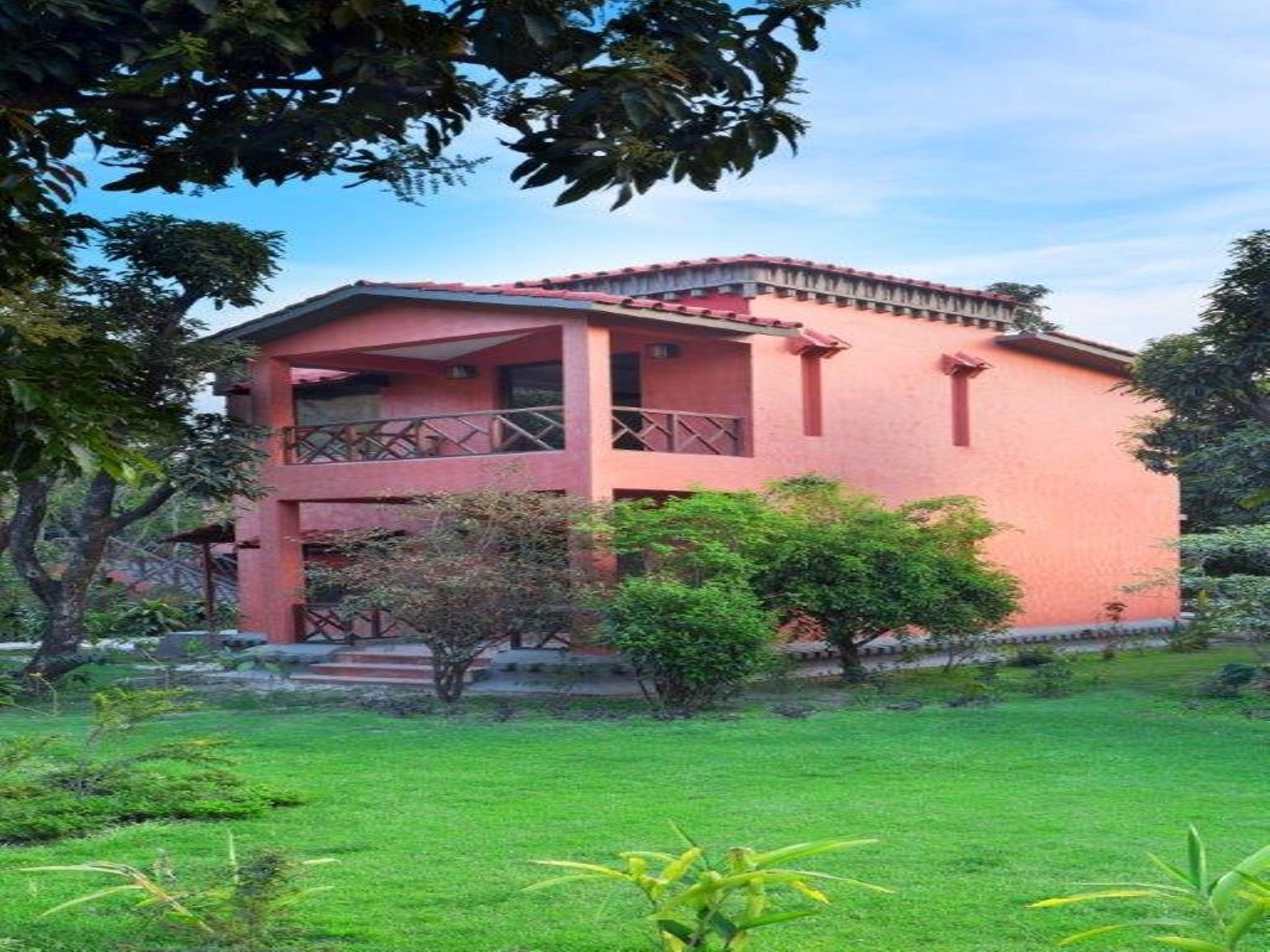 Um edifício de dois andares com varanda no andar superior, cercado por vegetação.