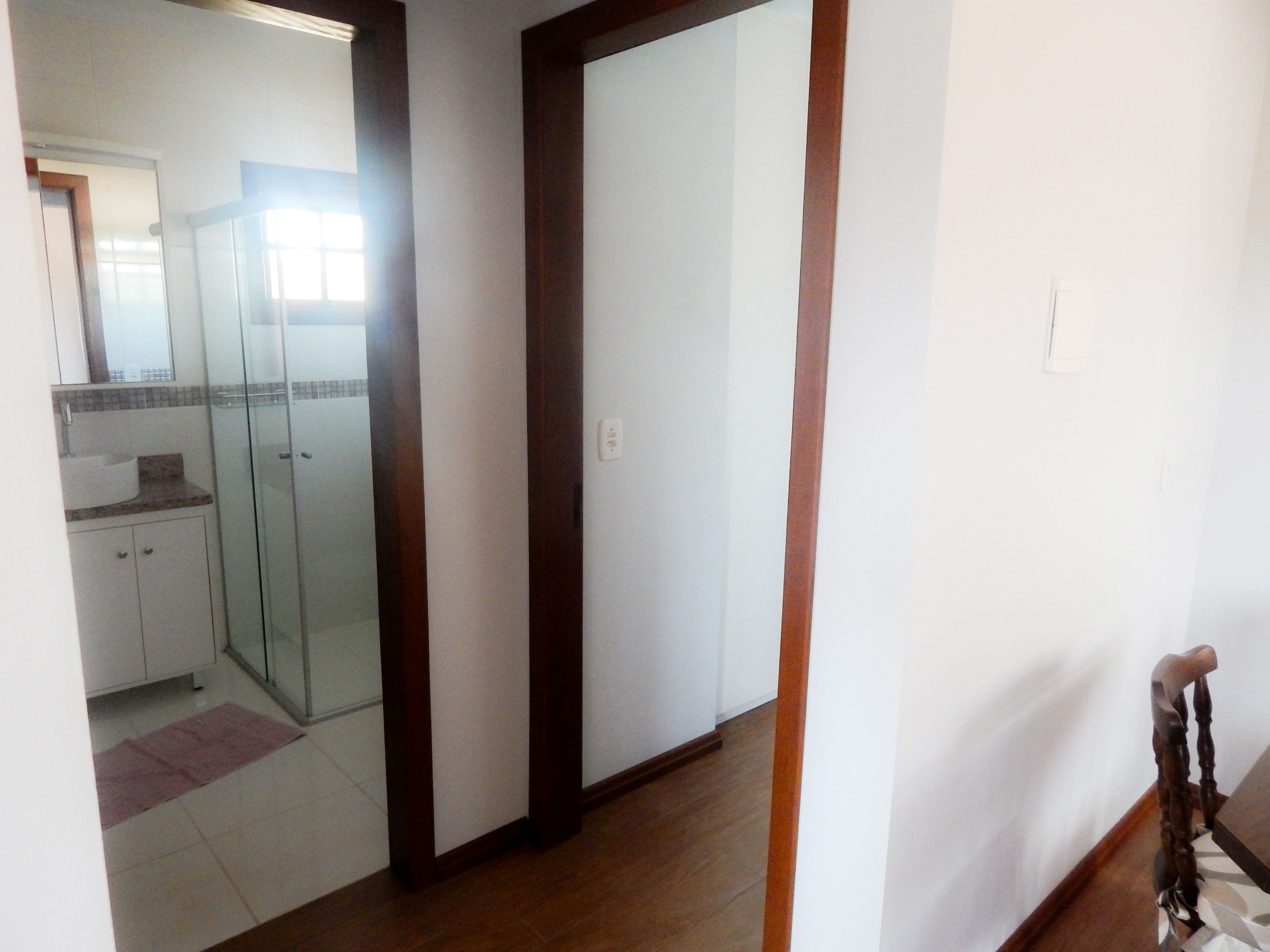 Um corredor com piso de madeira, box de vidro e porta branca.