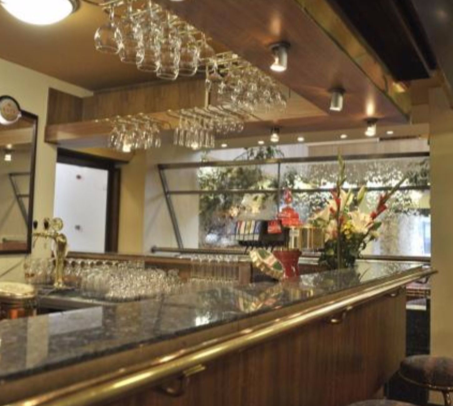 Uma área de bar com bancada de granito polido, lustres de cristal pendentes e vista para o exterior através de grandes janelas.