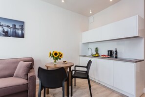 Uma cozinha moderna com armários brancos, bancada de madeira e um espaço de refeições com uma mesa redonda e duas cadeiras.