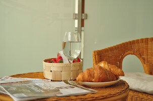 Uma mesa de vime com uma cesta contendo morangos, um copo de água e um croissant num prato.