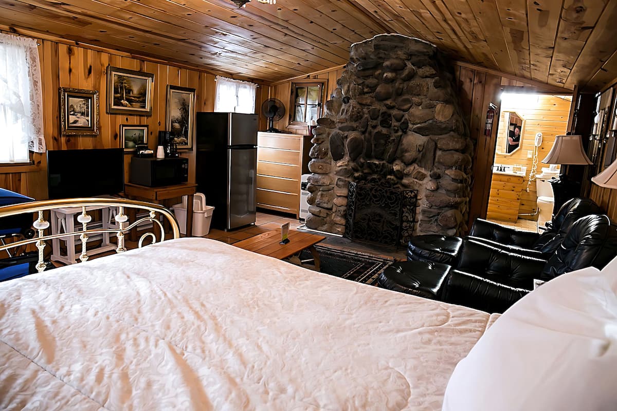 Um quarto acolhedor em estilo cabana, com uma cama, lareira de pedra, televisão e frigorífico.