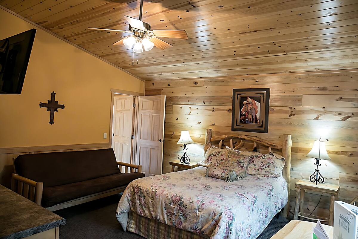 Quarto com painéis de madeira, uma cama, um sofá e uma escrivaninha.