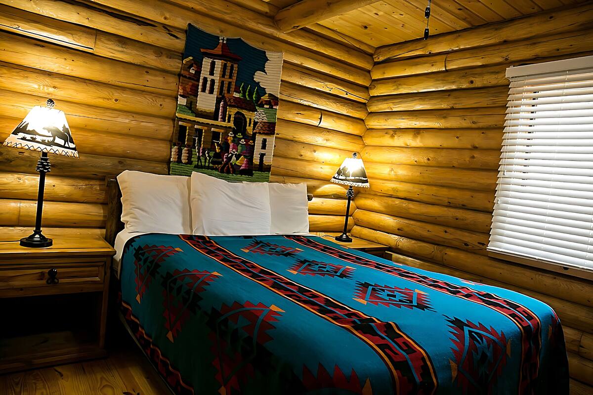 Quarto de cabana de madeira com uma cama, duas luminárias de cabeceira e uma janela com persianas.