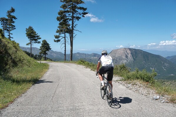 Um ciclista numa estrada pavimentada, com uma paisagem montanhosa ao fundo.
