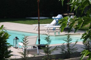 Área de piscina com espreguiçadeiras e uma pequena mesa, rodeada por vegetação.