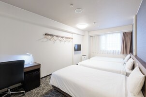 Quarto de hotel com duas camas, uma escrivaninha com luminária, uma televisão e um cabideiro.