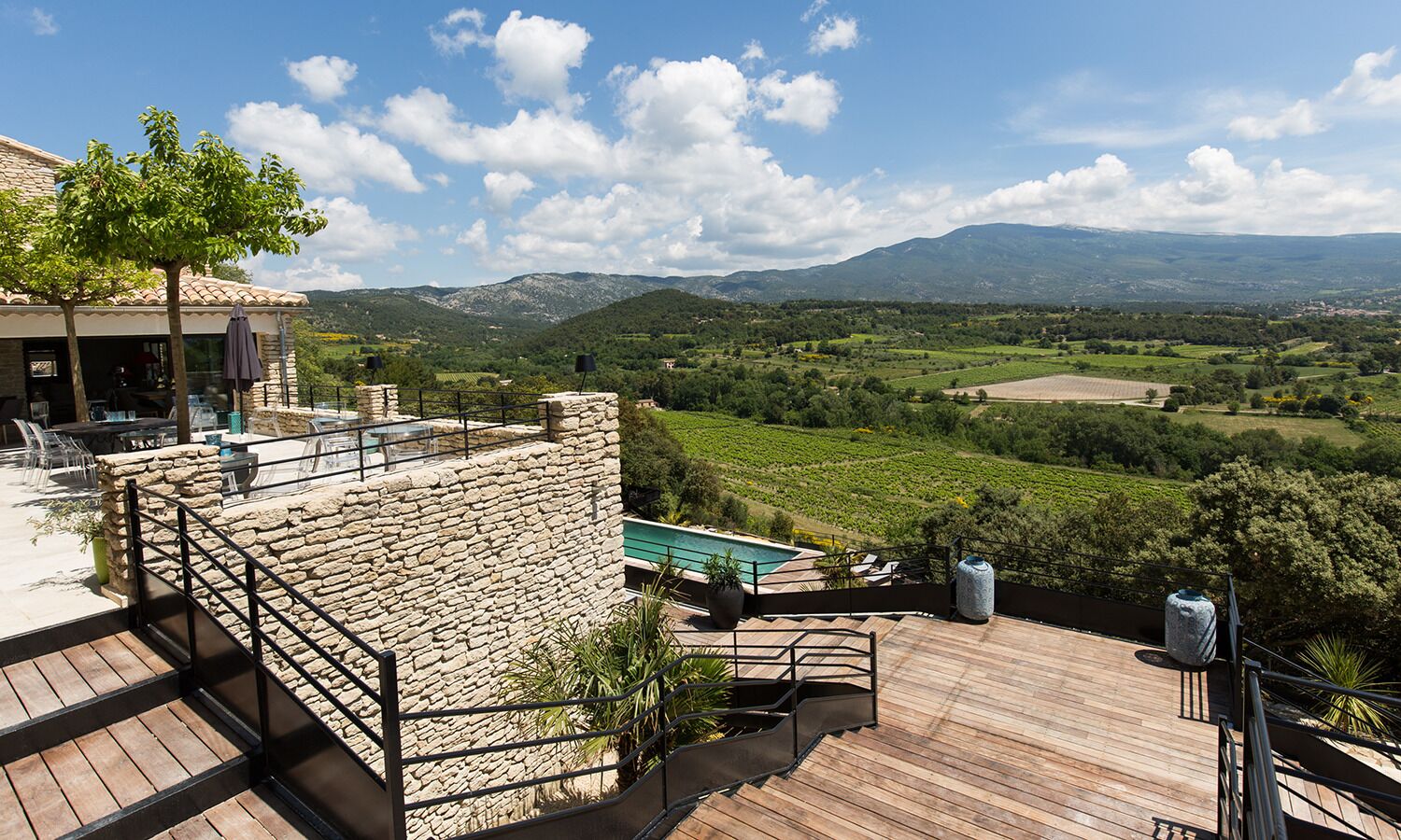 Terraço no telhado com parede de pedra, piscina e vista para vinhedos e montanhas.