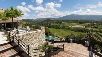Terraço no telhado com parede de pedra, piscina e vista para vinhedos e montanhas.