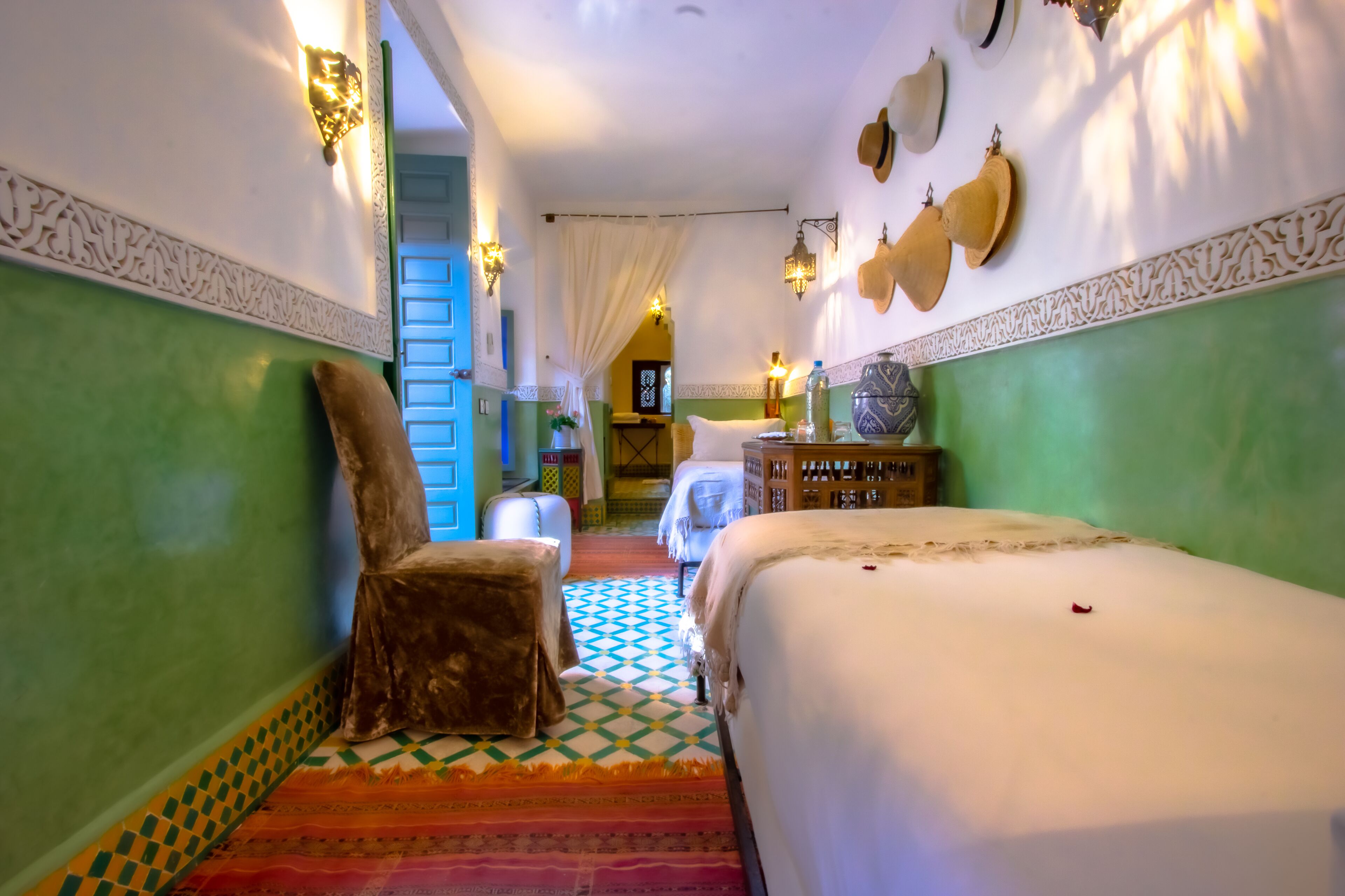 Quarto de hotel com uma cama, uma cadeira, uma mesinha e um detalhe decorativo na parede.