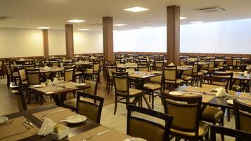 Uma grande sala de jantar com várias mesas e cadeiras dispostas em fileiras.
