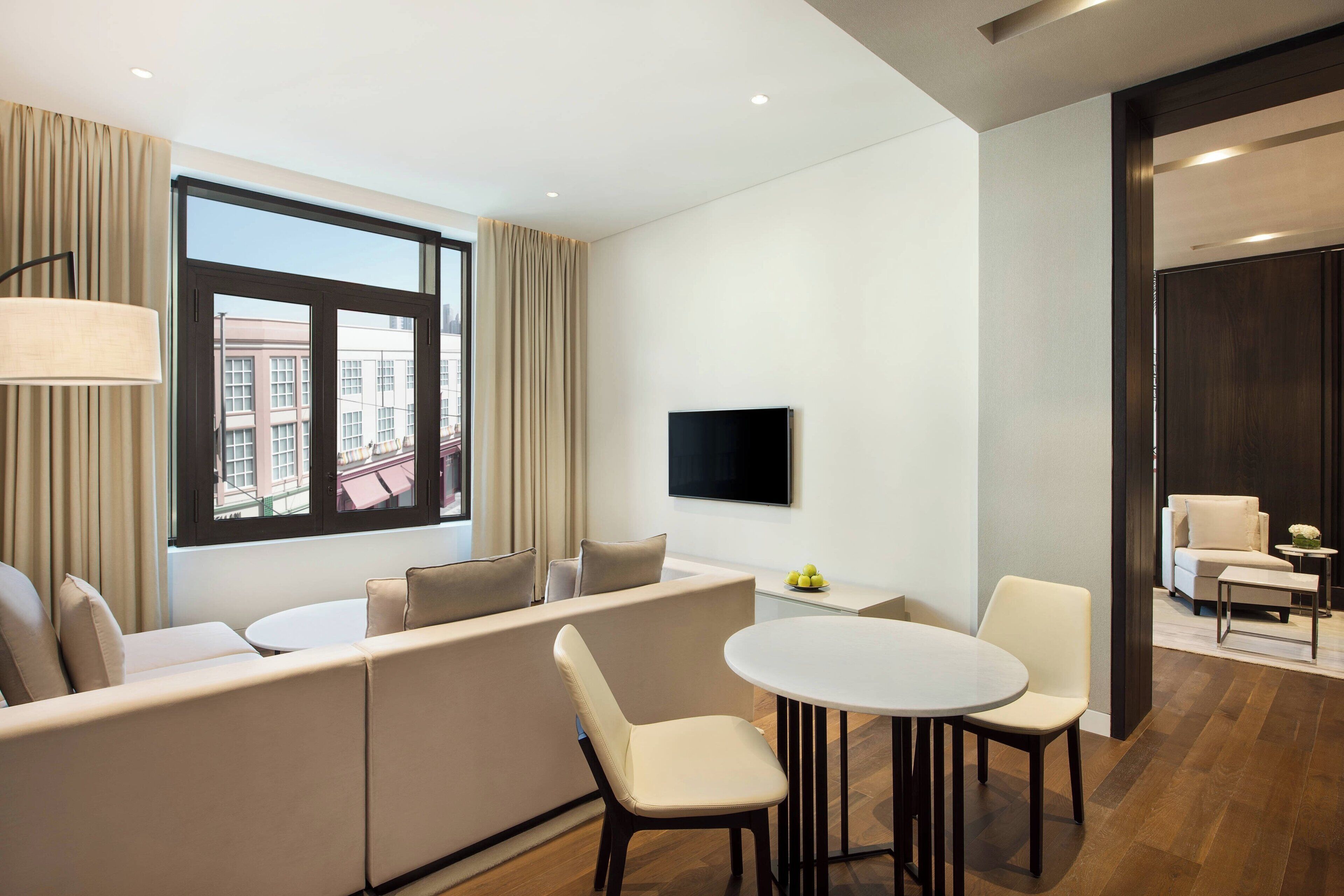 Quarto de hotel moderno com uma janela grande, televisão de tela plana, sofá, mesa de jantar e pequena mesa de centro.