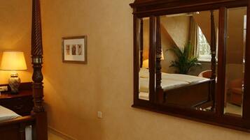 Quarto de hotel com um espelho grande, estrutura de cama de madeira, mesa de cabeceira com abajur e um quadro emoldurado na parede.