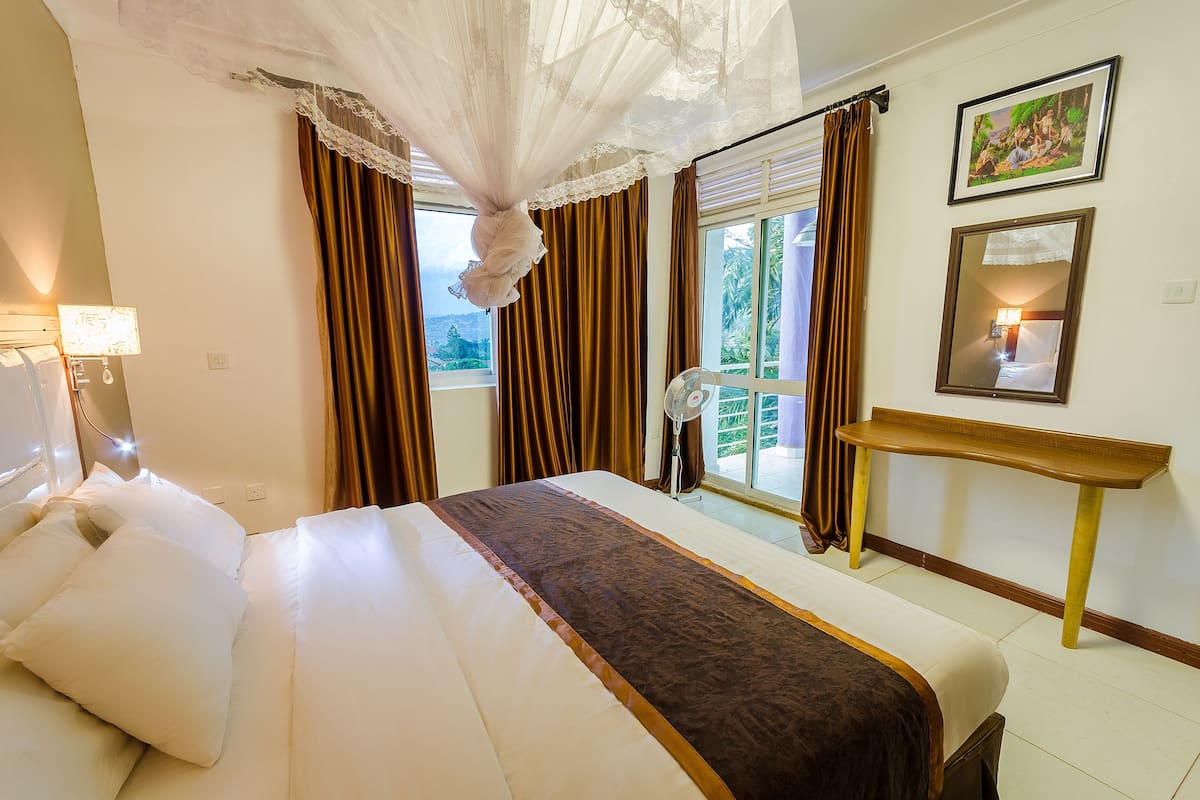Quarto de hotel com cama, cortinas, mesa de cabeceira, luminária e janela com vista.