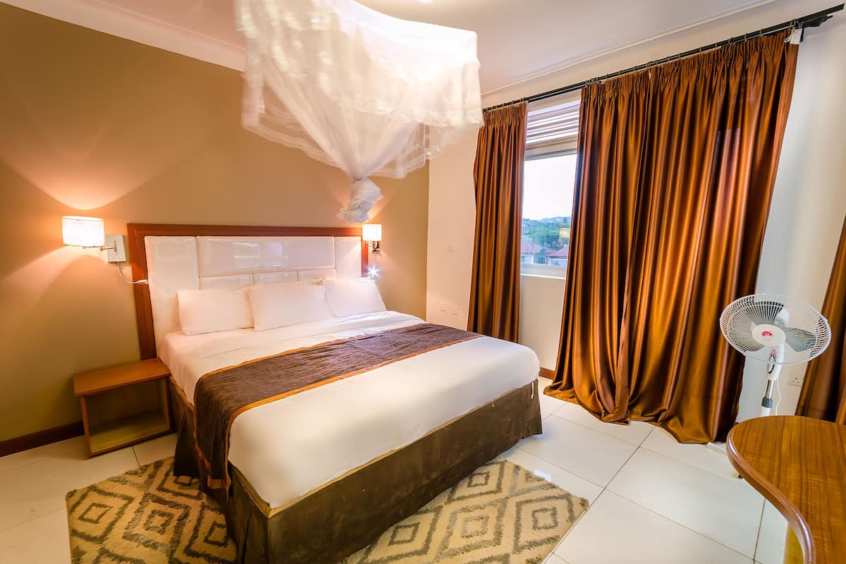 Quarto de hotel com cama, luminárias de cabeceira, um ventilador e uma janela com cortinas.