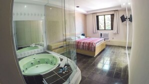 Quarto com jacuzzi envidraçada, cama com colcha estampada e janela com cortinas.