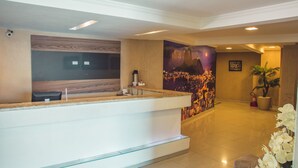 Uma área de recepção de hotel com um balcão moderno, um mural grande com vista para a cidade e um vaso de planta.