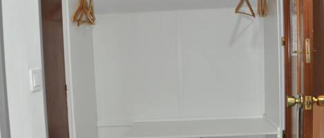 Um closet espaçoso com porta de madeira, uma estante branca e um pequeno móvel de gavetas branco.