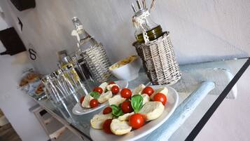Mesa de vidro com pratos de bruschetta e tomates cereja, rodeada por cestos de vime com garrafas de vidro.