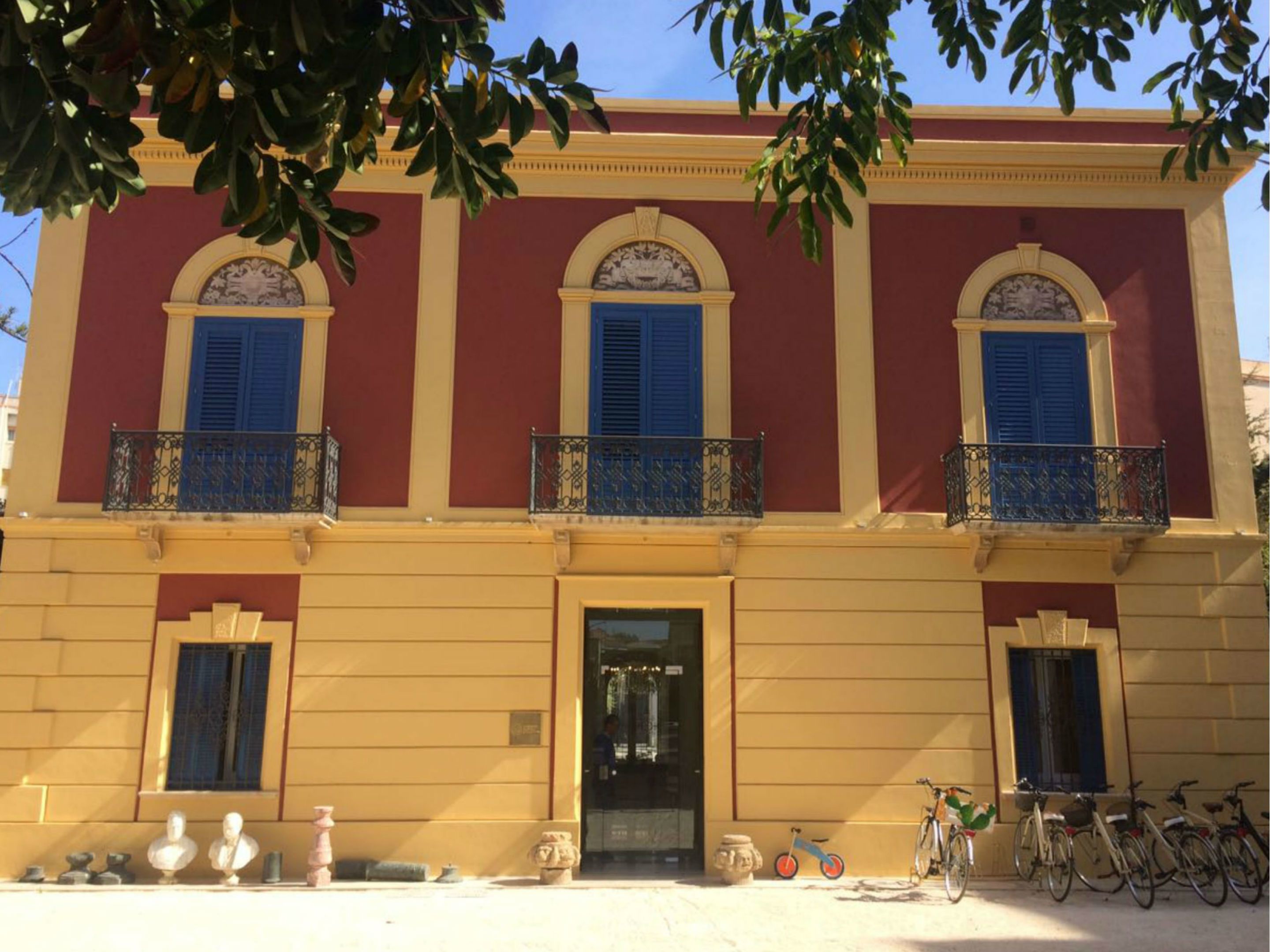 Um edifício com três janelas em arco, uma entrada central e varandas com grades de ferro forjado.