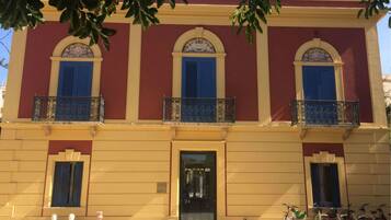 Um edifício com três janelas em arco, uma entrada central e varandas com grades de ferro forjado.