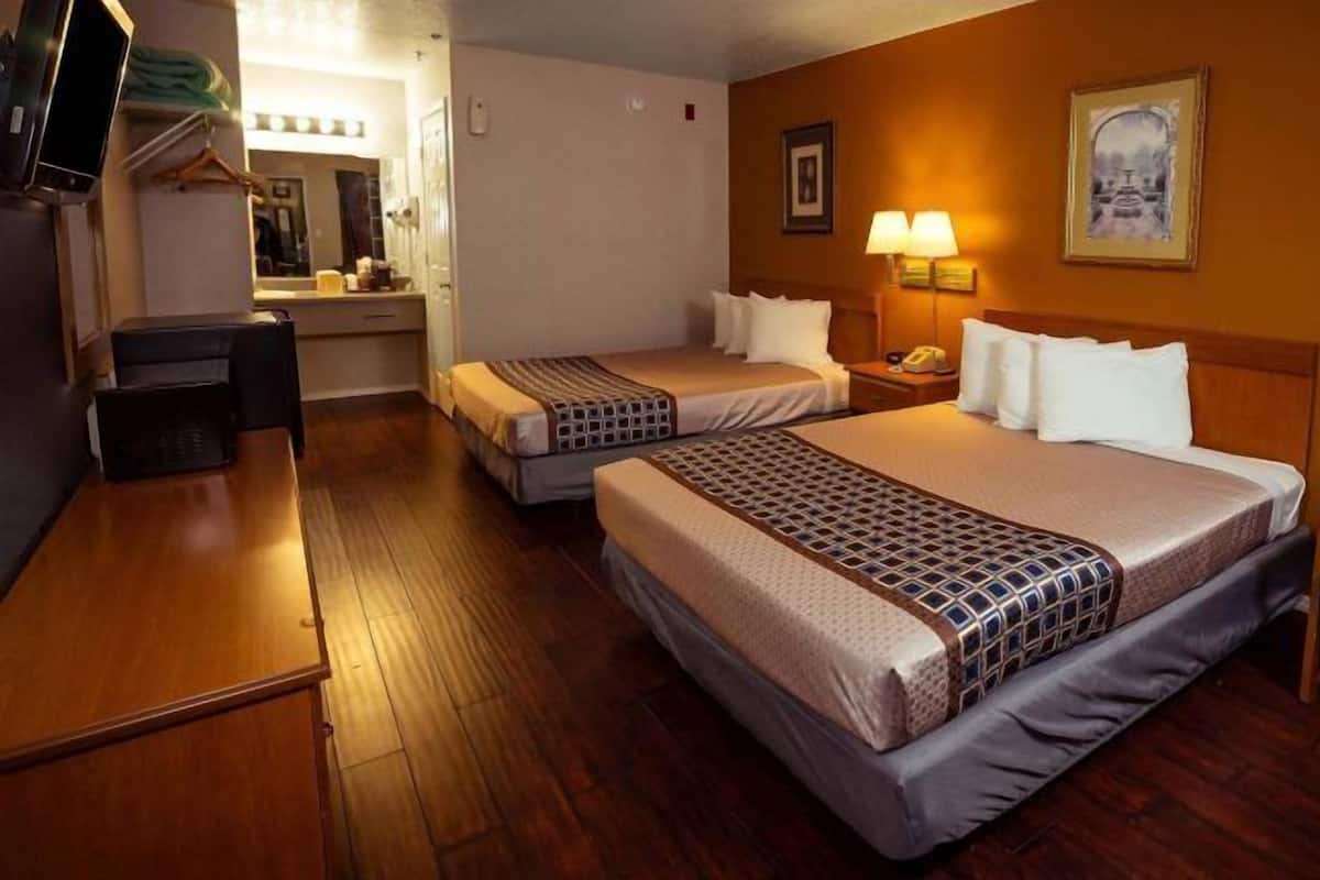 Quarto de hotel com duas camas, uma mesa, uma cadeira e um espelho.