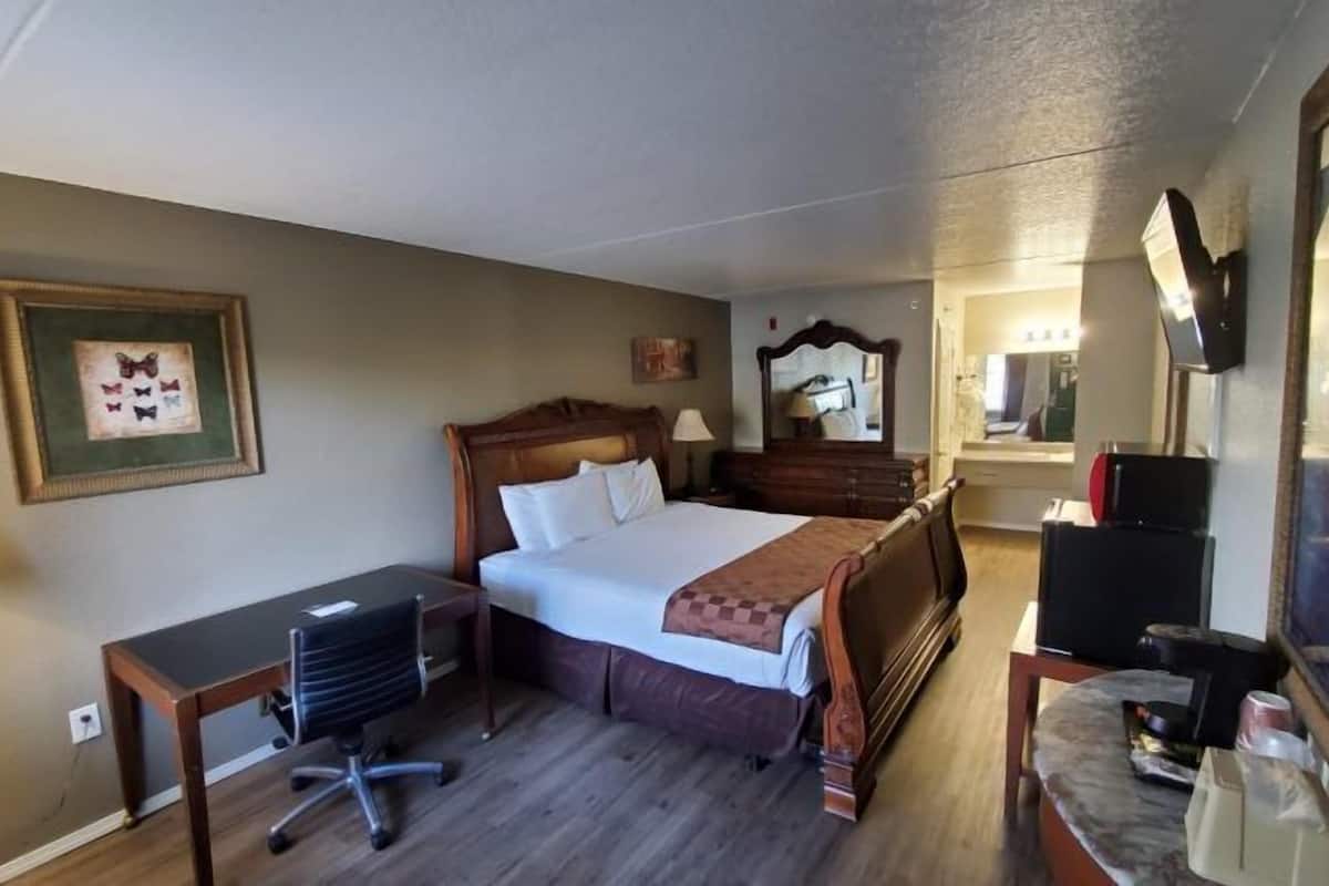 Quarto de hotel com cama, escrivaninha, cadeira e espelho.
