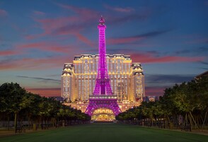 Um hotel grande com uma torre imponente que lembra a Torre Eiffel, rodeado por um gramado bem cuidado e árvores.