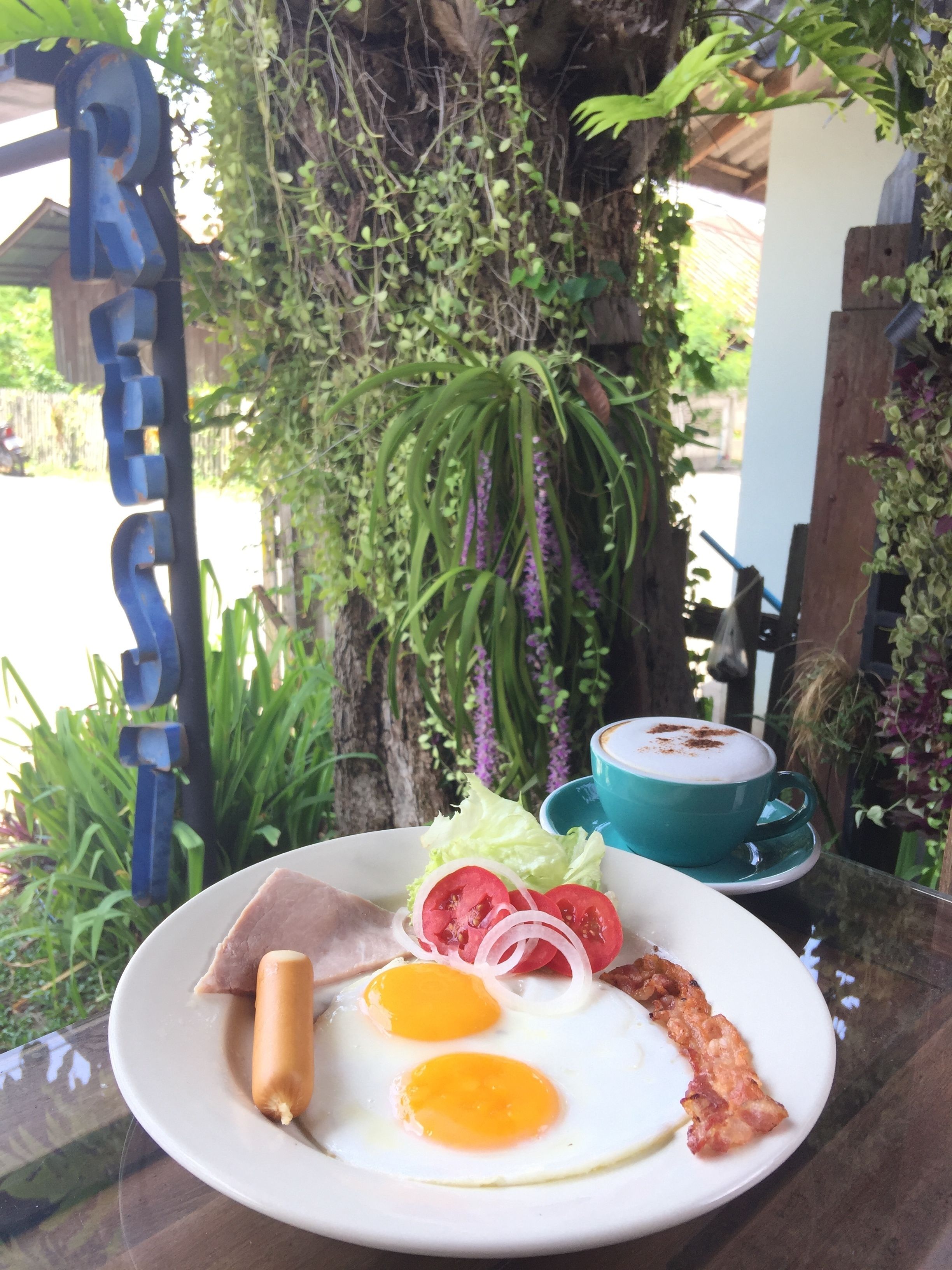 Prato de café da manhã com ovos, bacon e tomates sobre uma mesa, com uma xícara de café.