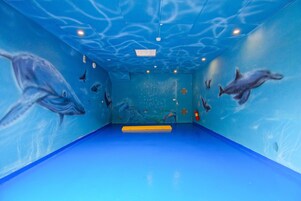 Piscina interna com murais de golfinhos nas paredes e piso azul.