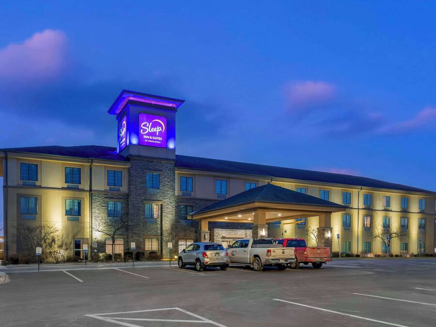 Um hotel com uma placa visível, vários espaços de estacionamento e uma entrada bem iluminada.