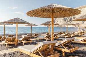 Na praia, areia preta, espreguiçadeiras, guarda-sóis 