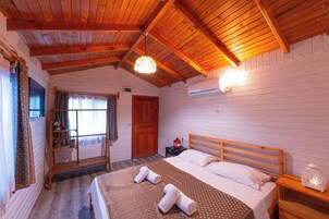 Quarto com painéis de madeira, uma cama, uma mesinha de cabeceira, uma prateleira e uma janela com cortinas.