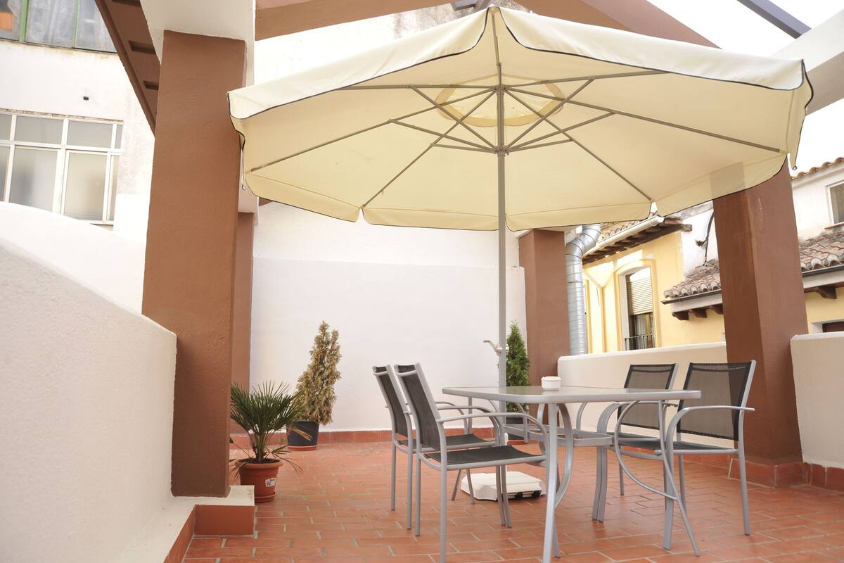 Um pátio externo com mesa e cadeiras sob um grande guarda-sol.