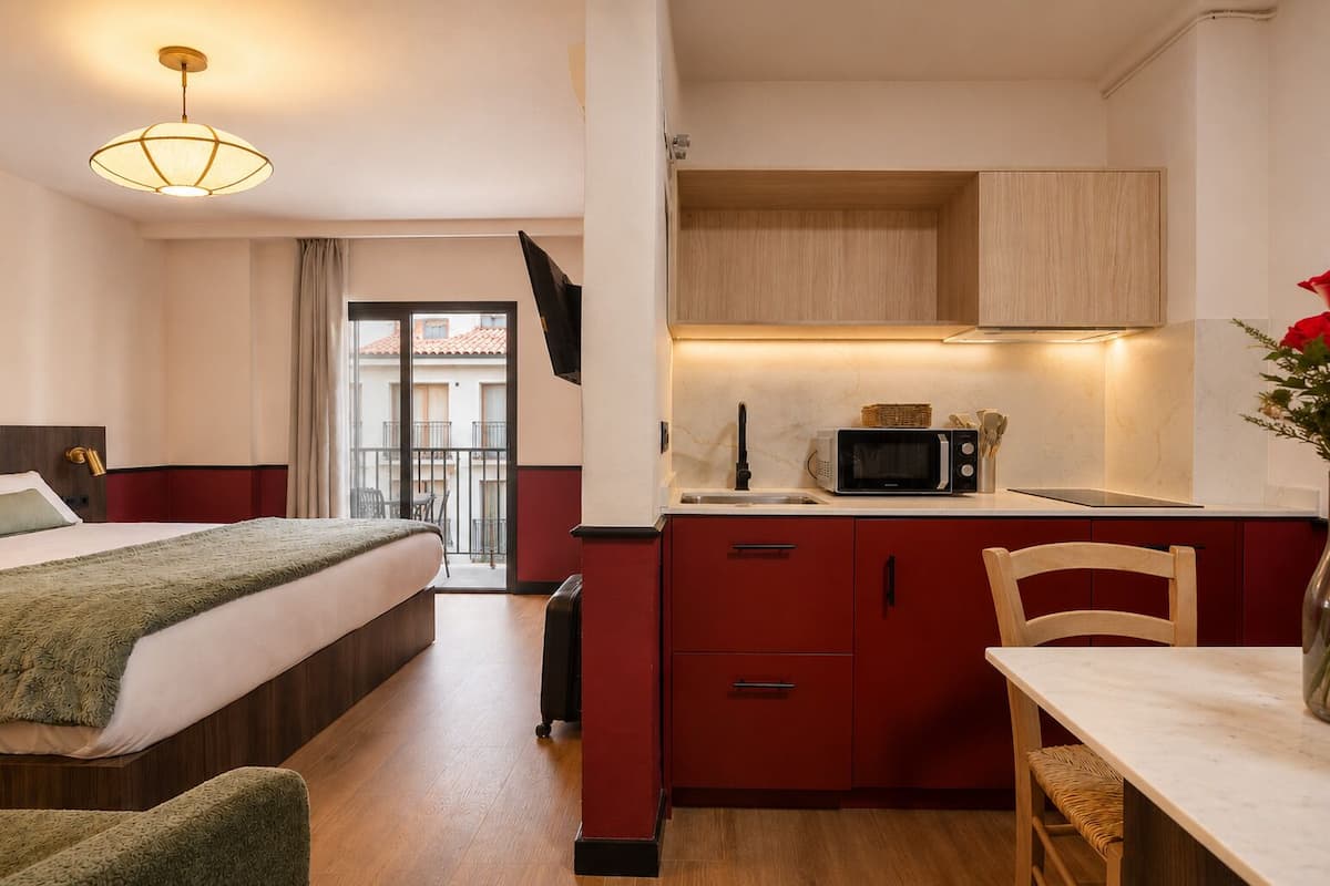 Quarto de hotel com cama, pequena cozinha, área de refeições e varanda com vista.