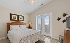 Quarto com uma cama grande, um ventilador de teto, uma janela com vista e uma parede decorada com tartarugas.