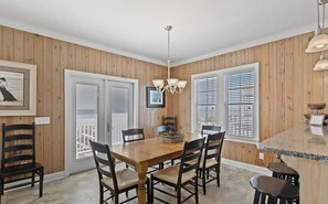Uma sala de jantar com uma mesa e cadeiras de madeira, um candelabro e vista para o exterior.
