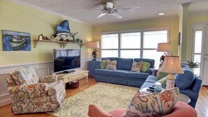 Uma sala de estar com televisão, dois sofás, um tapete estampado e objetos decorativos em prateleiras.